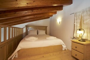 Quarto com cama de madeira, mesa de cabeceira, abajur e janela com cortinas.