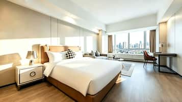 Quarto de hotel moderno com uma cama grande, uma escrivaninha e vista para o horizonte da cidade.
