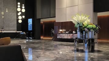 Um lobby moderno com balcão de recepção, área de estar e um arranjo floral decorativo.