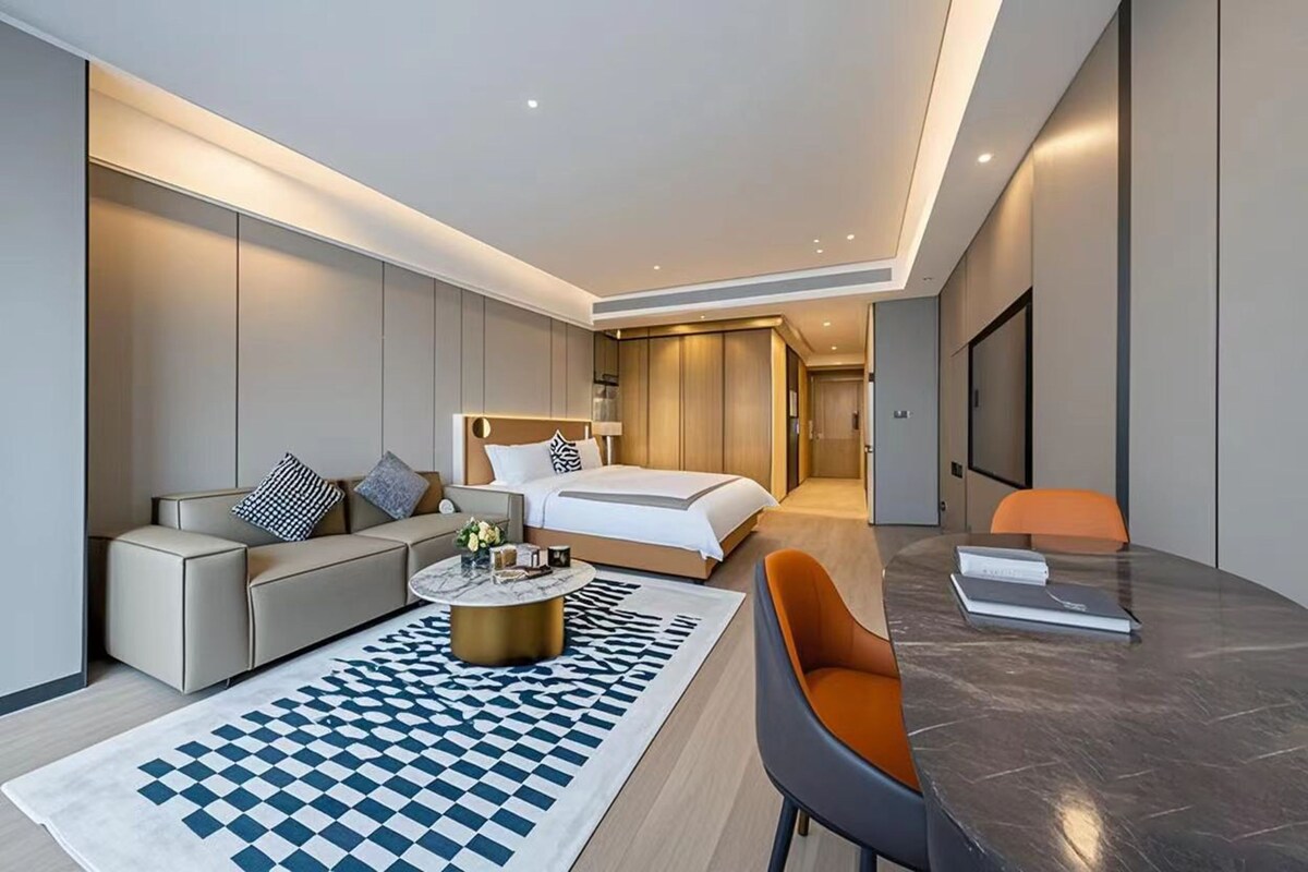 Quarto de hotel moderno com sofá, cama, mesa de centro e televisão.