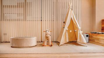 Quarto com uma janela grande, piso de madeira, cama redonda, um pequeno brinquedo de cavalo de madeira e um tipi branco.