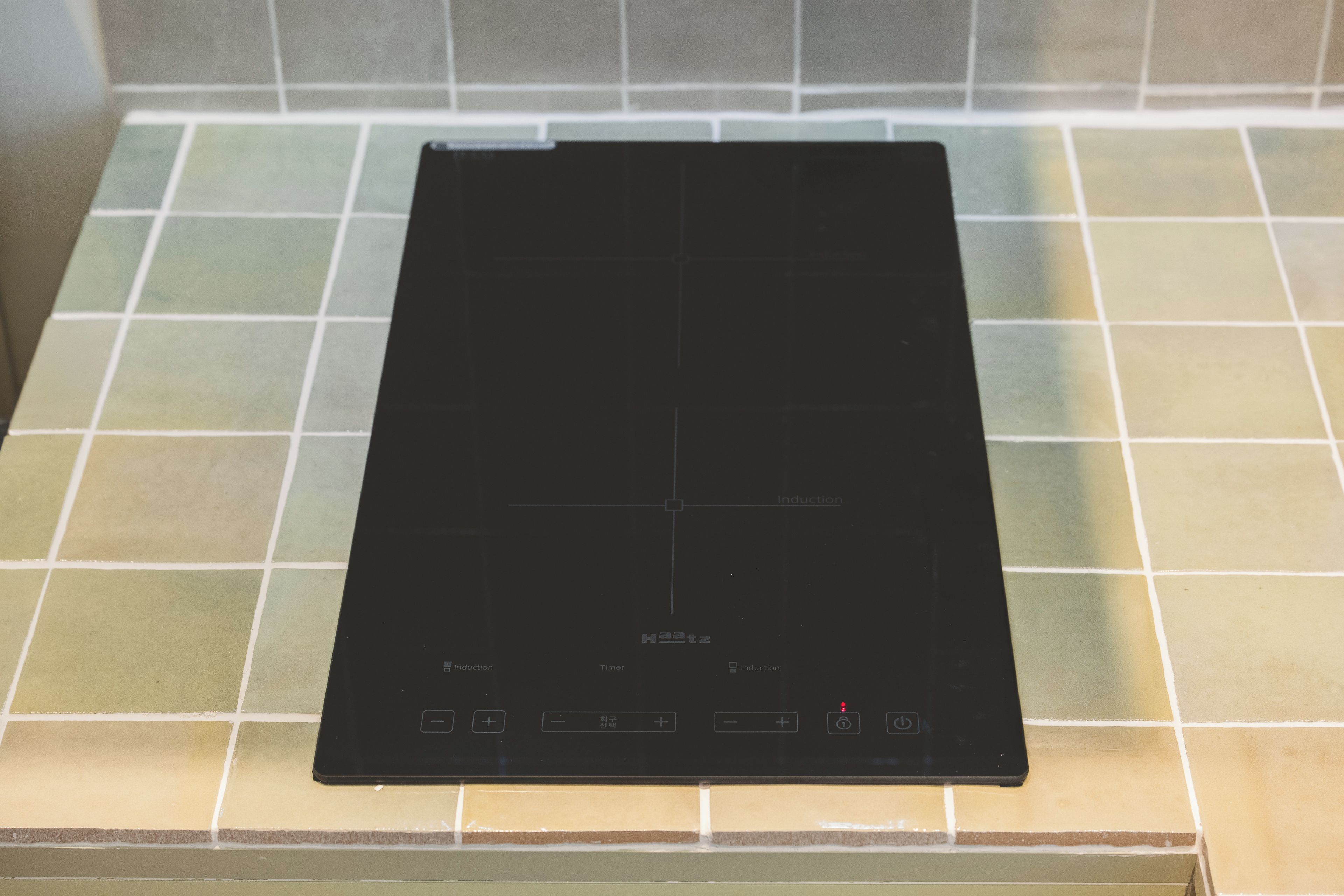 Um fogão por indução preto sobre uma bancada de cozinha revestida com azulejos.