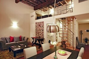 Uma sala de estar ampla, com teto alto, escada e um espaço de jantar com mesa e cadeiras.