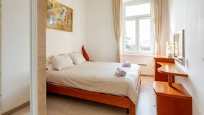 Quarto com cama, mesa de cabeceira de madeira, janela com cortinas e um quadro na parede.