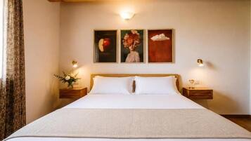 Quarto de hotel com uma cama grande, duas mesas de cabeceira e três quadros pendurados na parede.