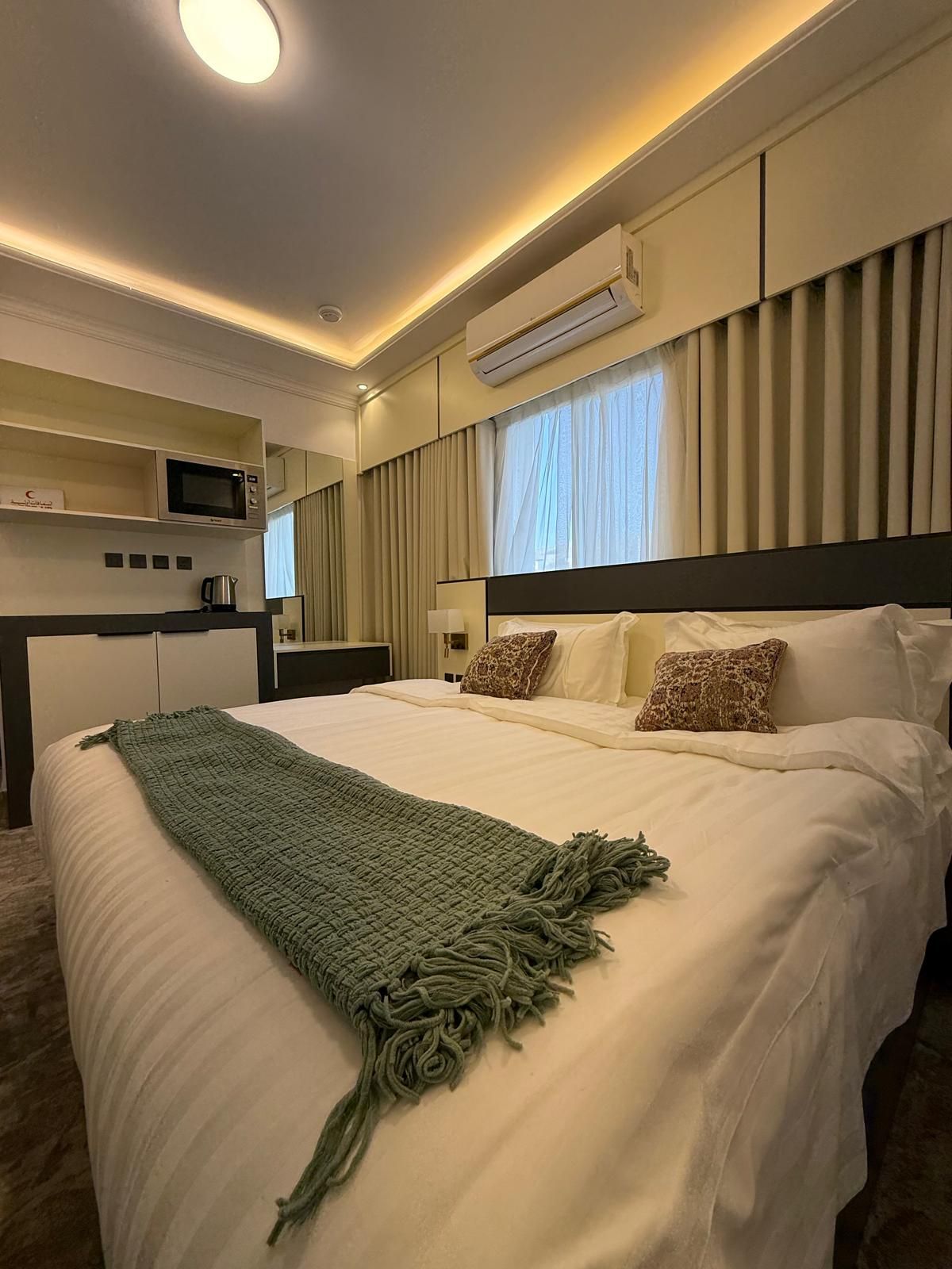 Quarto de hotel com cama grande, micro-ondas, pequeno espaço de cozinha e aparelho de ar condicionado.