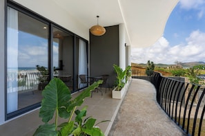 Uma varanda com vista para o mar, uma mesa com cadeiras e plantas em vasos.