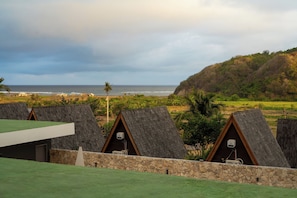 Fileira de cabanas com telhados triangulares e paredes de pedra, com vista para uma praia e oceano.