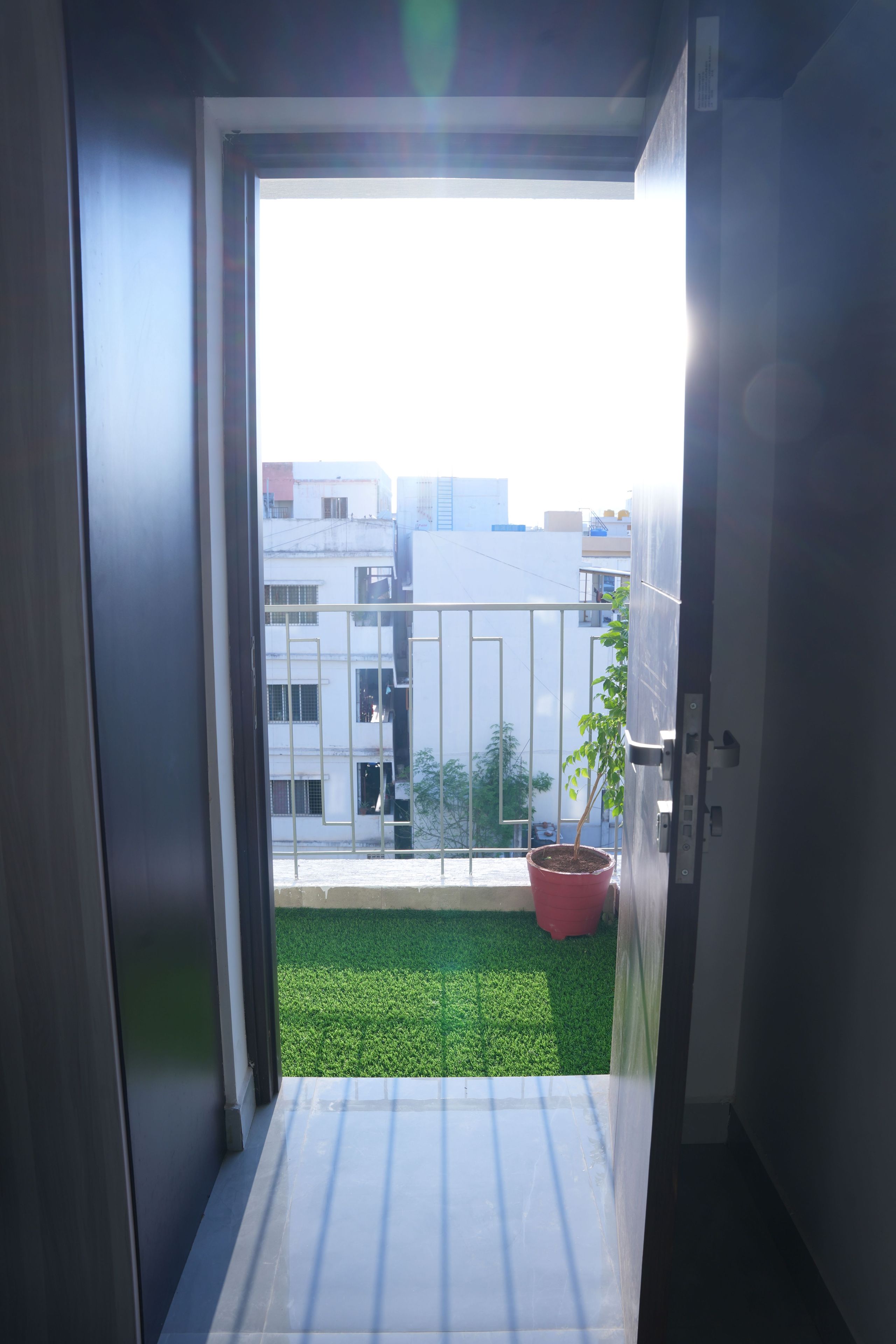 Uma porta dá acesso a uma varanda com um pequeno tapete de grama sintética e um vaso de planta.