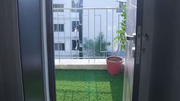 Uma porta dá acesso a uma varanda com um pequeno tapete de grama sintética e um vaso de planta.