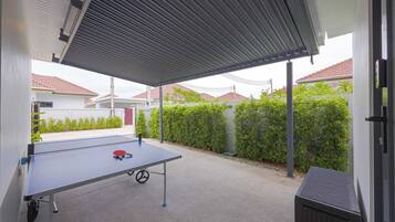 Mesa de pingue-pongue ao ar livre, sob uma cobertura, com vista para um bairro residencial.