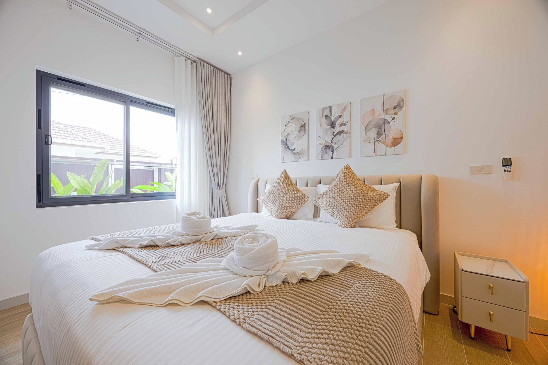 Quarto de hotel com uma cama grande, mesa de cabeceira, janela com cortinas e obras de arte na parede.