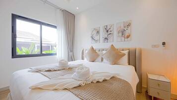Quarto de hotel com uma cama grande, mesa de cabeceira, janela com cortinas e obras de arte na parede.