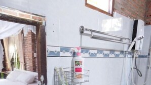 Uma casa de banho com uma pia branca, uma prateleira de vidro com produtos de higiene pessoal, zona de duche e uma janela com vista para um muro de tijolos.
