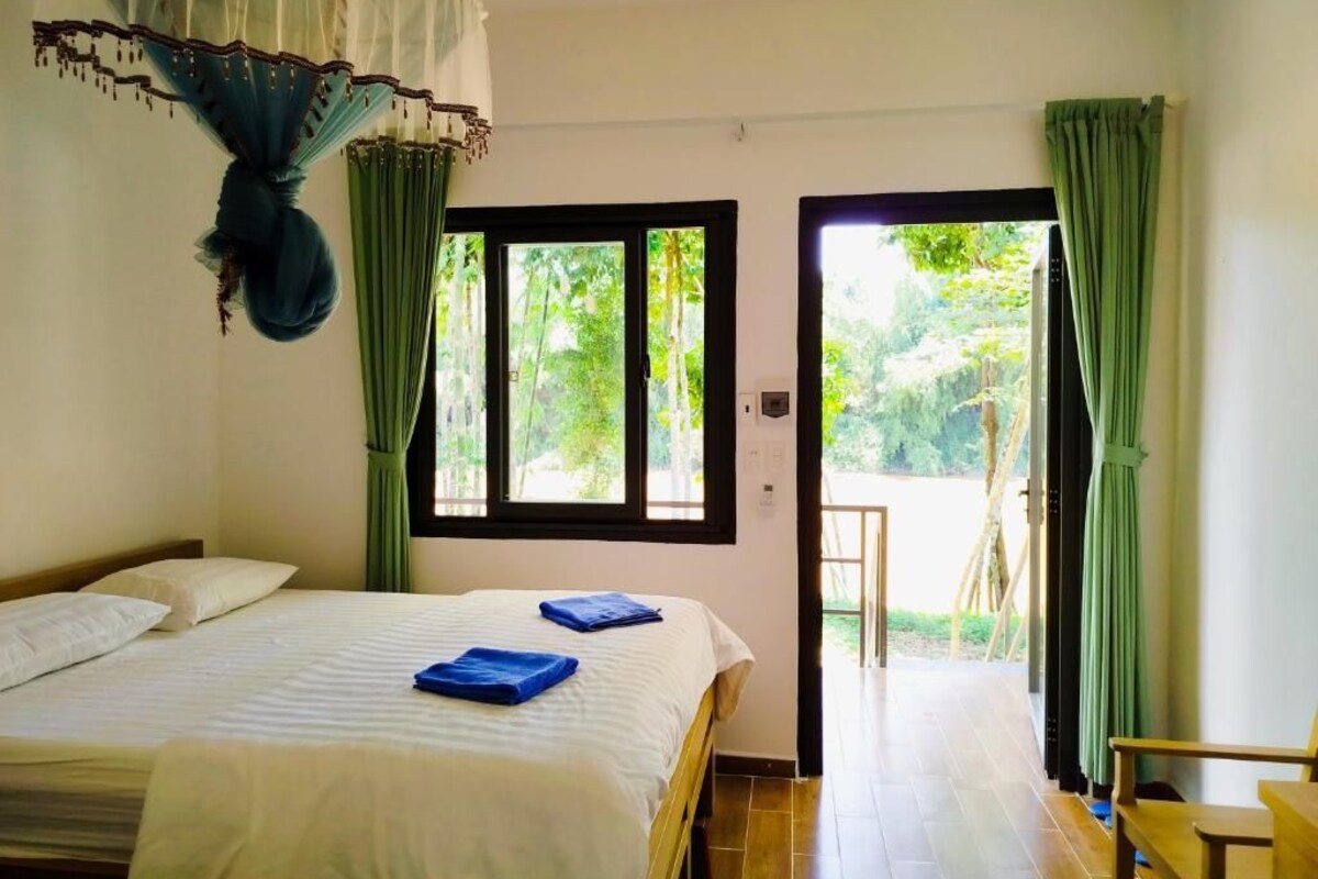 Quarto com cama, duas janelas, porta para uma varanda e uma cadeira.