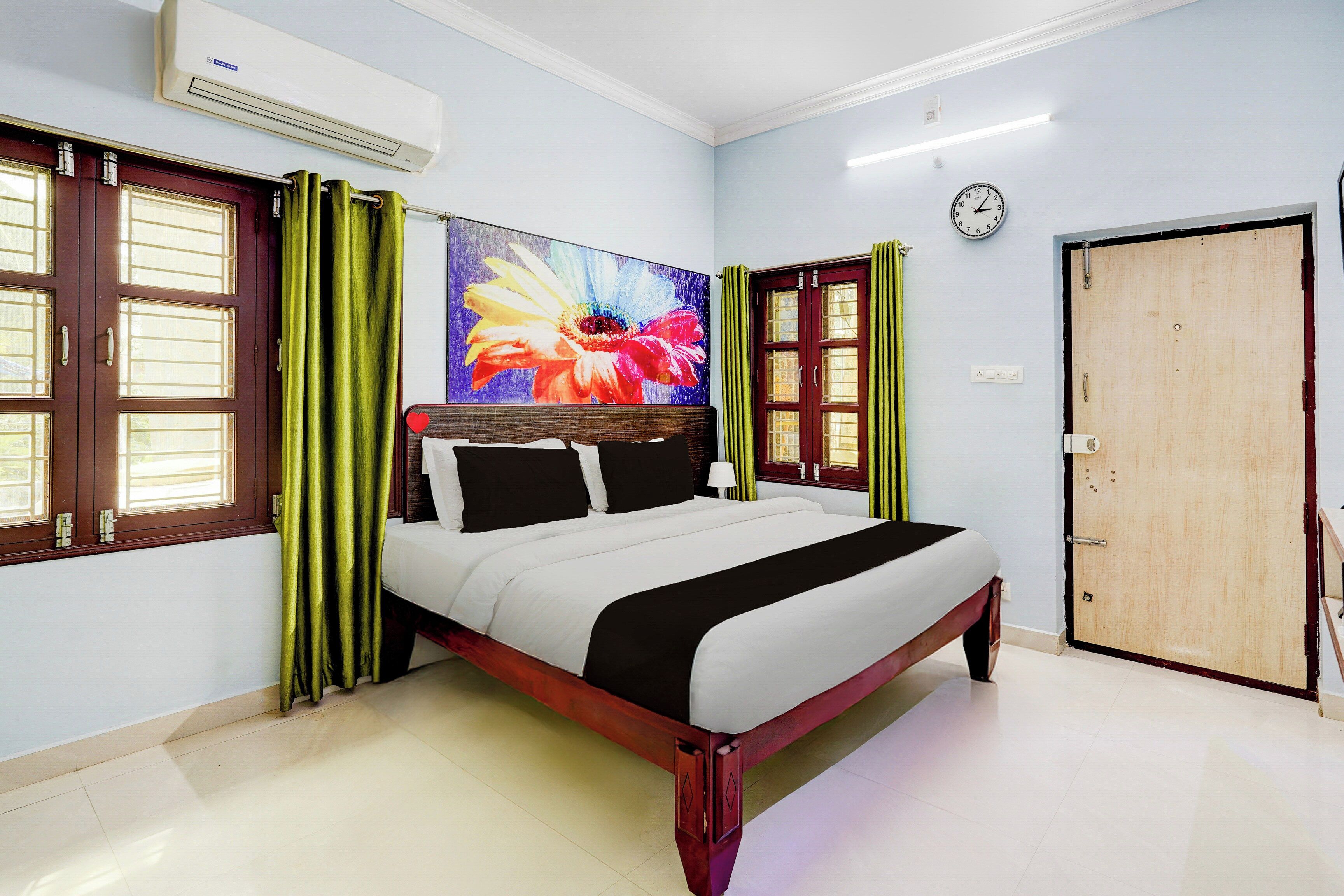 Quarto com cama, cortinas, um quadro, relógio e ar condicionado.