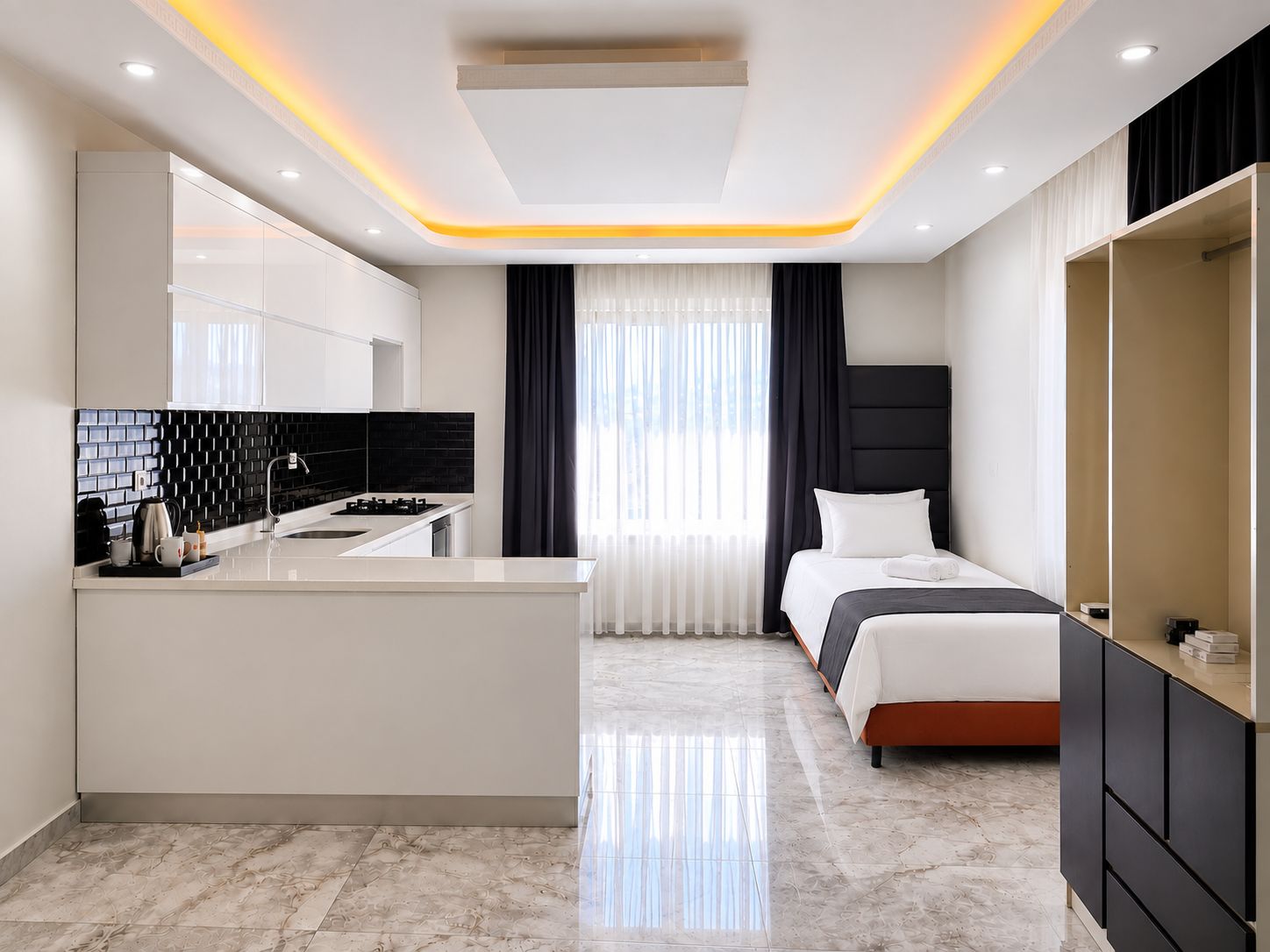 Quarto de hotel moderno com cozinha, cama com cabeceira e roupeiro embutido.