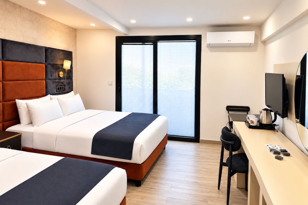 Quarto de hotel com duas camas, uma escrivaninha com cadeira, televisão e ar condicionado.