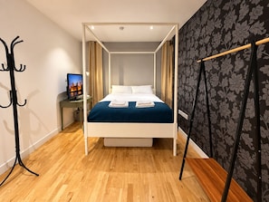 Quarto moderno com cama de dossel, televisão num criado-mudo e cabideiro.