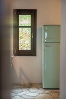 Quarto com piso de pedra, geladeira verde e janela com vista para vegetação.