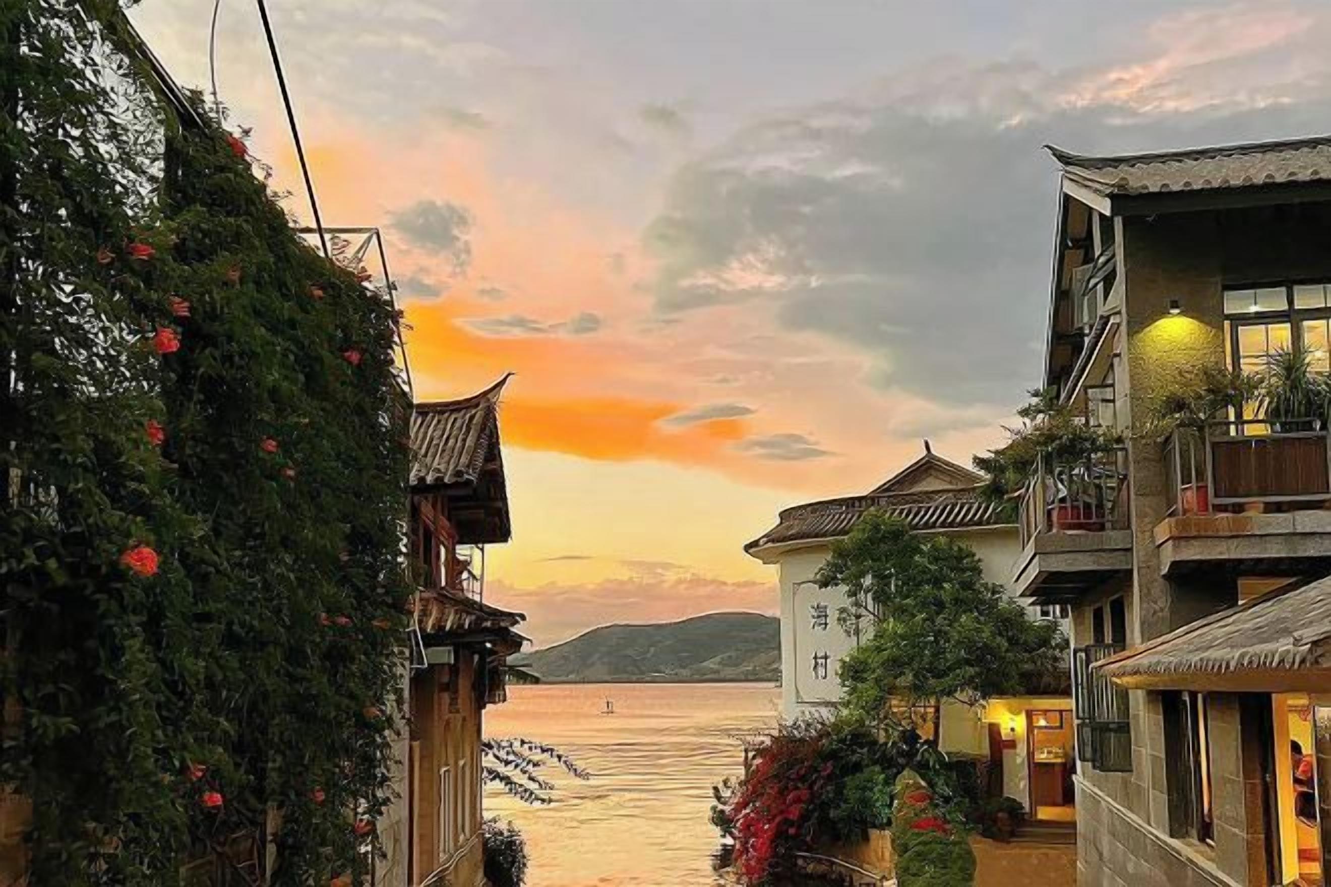 Um edifício tradicional com varanda, vista para um corpo d'água e um pôr do sol ao fundo.