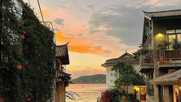 Um edifício tradicional com varanda, vista para um corpo d'água e um pôr do sol ao fundo.