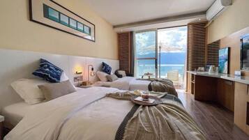 Quarto de hotel com duas camas, televisão, escrivaninha e vista para o mar.