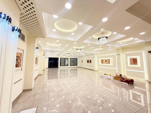 Um hall de hotel espaçoso com piso de mármore polido, iluminação embutida e um candelabro.