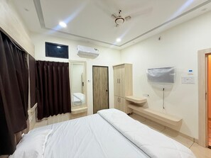 Quarto de hotel com cama, televisão, ar condicionado, guarda-roupa e espelho de banheiro.