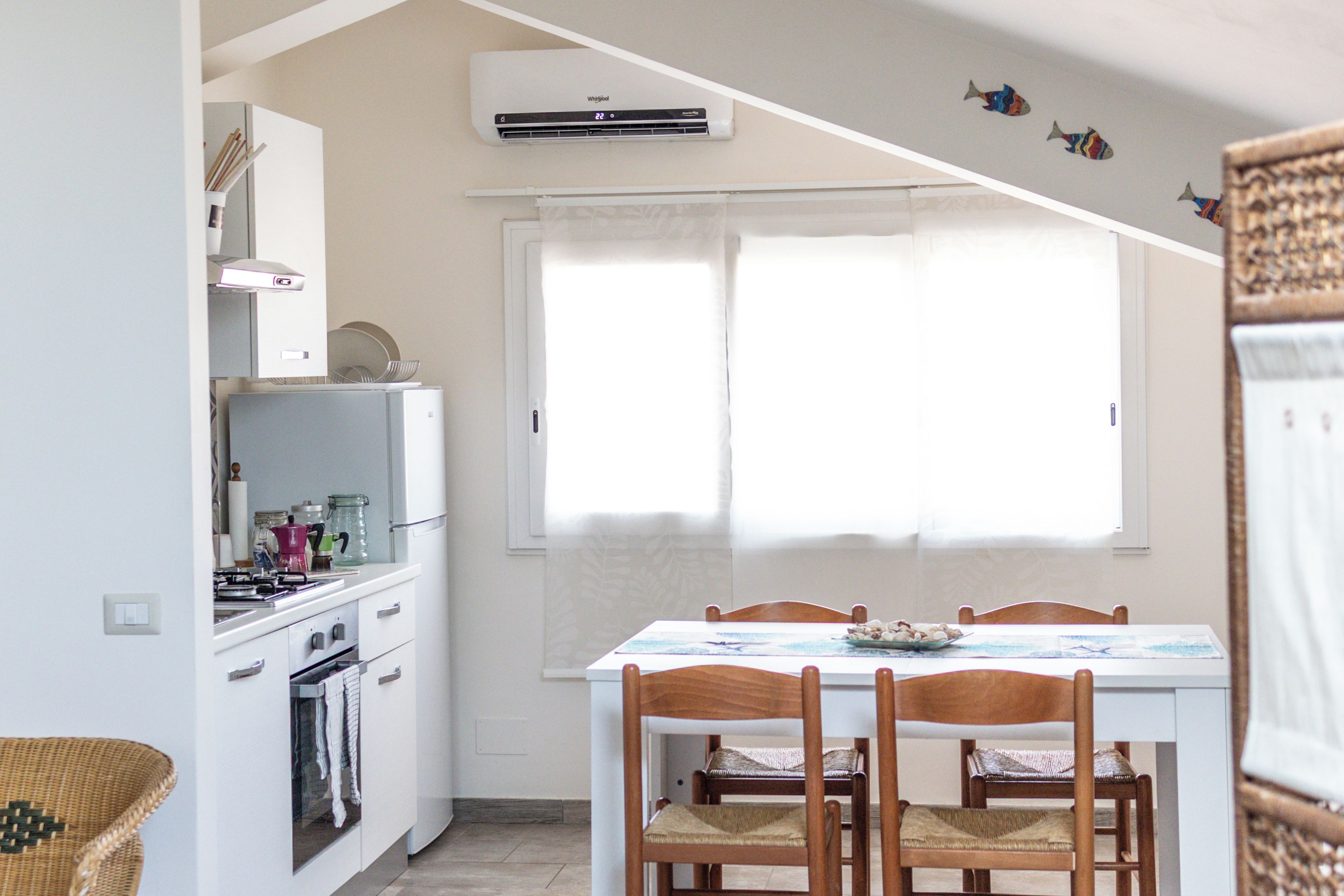 Cozinha compacta com mesa e cadeiras, ar-condicionado e janela com cortinas.