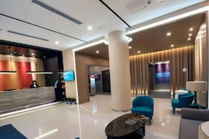 Um saguão de hotel moderno com balcão de recepção, área de estar e um pilar grande.