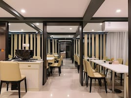 Um saguão de hotel moderno, com balcão de recepção, área de estar e um corredor longo que leva à área de refeições.