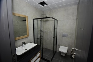 Casa de banho moderna com cabine de chuveiro em vidro, lavatório branco e sanita.