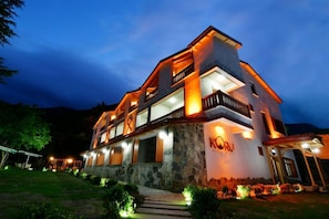 Um hotel com vários andares, fachada de pedra, varandas e uma entrada bem iluminada.
