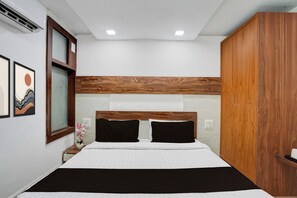 Quarto com cama, cabeceira de madeira, duas mesas de cabeceira, um criado-mudo, ar-condicionado fixado na parede e obras de arte emolduradas.