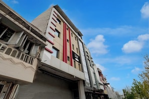 Edifício moderno de vários andares, com uma faixa vermelha vertical marcante e uma placa indicando uso comercial.