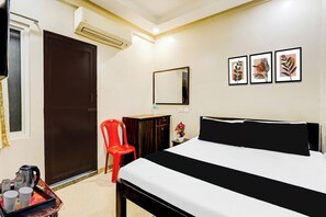 Quarto de hotel com cama, cadeira, escrivaninha, espelho e obras de arte nas paredes.