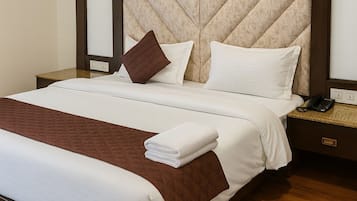Quarto de hotel com uma cama grande, cabeceira com padrão geométrico, mesa de cabeceira com telefone e piso de madeira.
