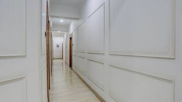 Um corredor com paredes brancas e piso de madeira, que leva a um quarto com porta.