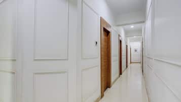 Corredor com paredes brancas, portas de madeira e chão de azulejos.