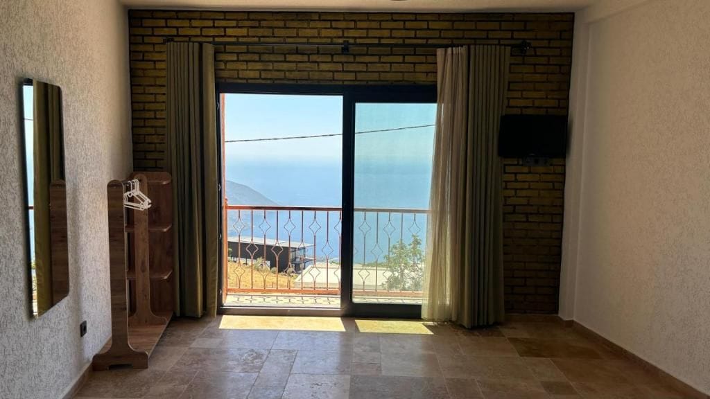 Quarto com uma grande porta de vidro que se abre para uma varanda com vista para o mar.