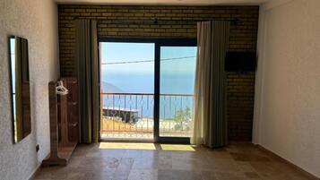 Quarto com uma grande porta de vidro que se abre para uma varanda com vista para o mar.