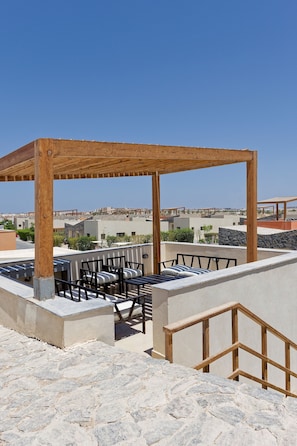 Terraço no telhado com pérgola de madeira, área de estar externa e piso de pedra.