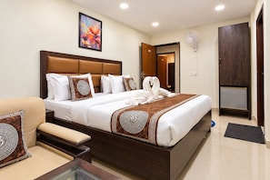 Quarto de hotel com cama, mesa de cabeceira, poltrona, guarda-roupa e ventoinha.