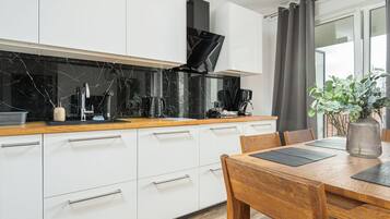 Cozinha moderna com armários brancos, fogão preto e área de jantar com mesa e cadeiras de madeira.