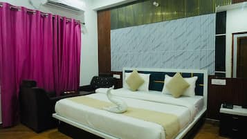 Quarto de hotel com cama, cadeira, escrivaninha e janela com cortinas.