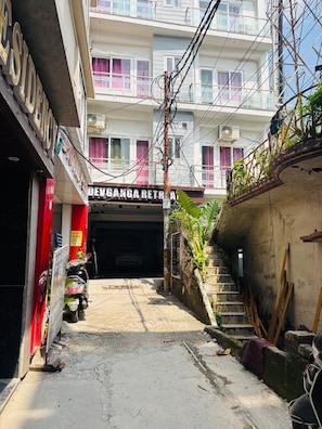 Uma rua estreita com um edifício identificado como 'DEVANGA RETREAT' e uma scooter estacionada.