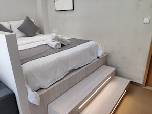 Quarto de hotel moderno com uma cama, um conjunto de degraus que levam à cama e uma luminária fixada na parede.