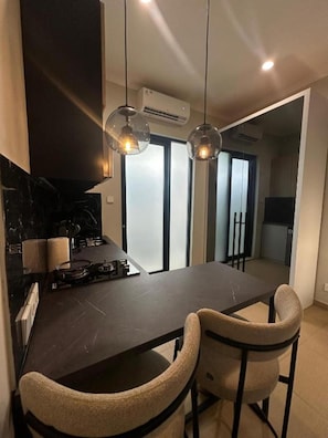 Cozinha moderna com bancada escura, duas luminárias pendentes e área de jantar com mesa e cadeiras.