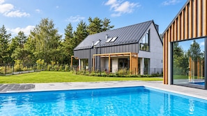Uma casa moderna com piscina, cercada por um gramado bem cuidado e árvores.